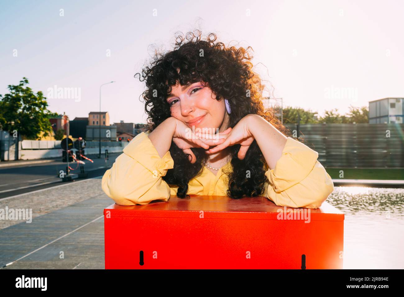Smiling woman with hand on chin leaning over metal box Stock Photo - Alamy