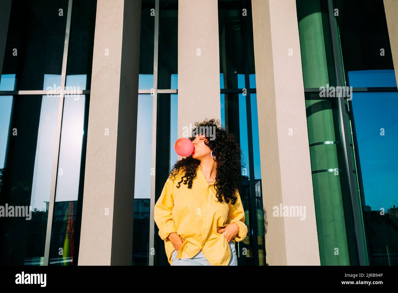 Woman blowing bubble gum in front of building on sunny day Stock Photo ...