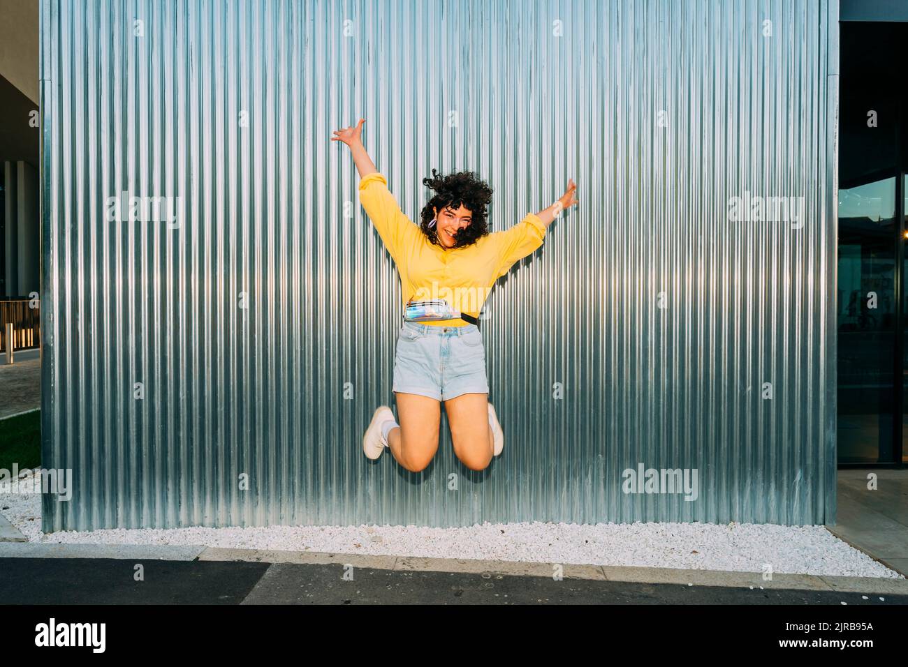 Cheerful woman jumping in front of corrugated wall Stock Photo - Alamy