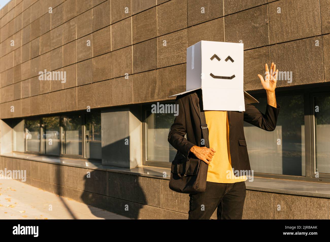 Businessman wearing box with smiley face waving hand at footpath on ...