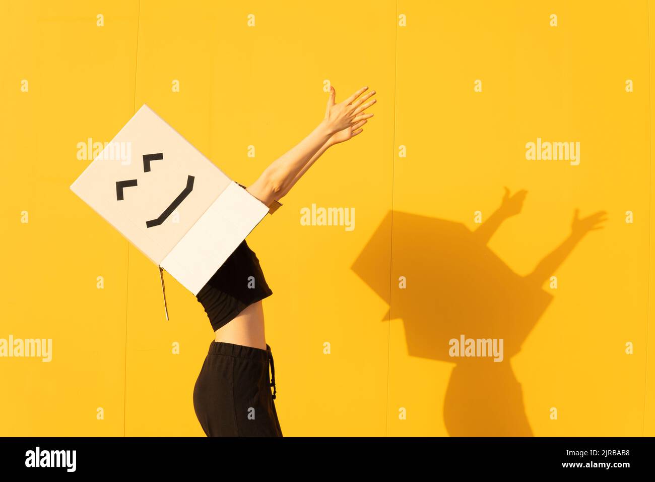 Happy woman wearing box with smiley face dancing by yellow wall Stock ...