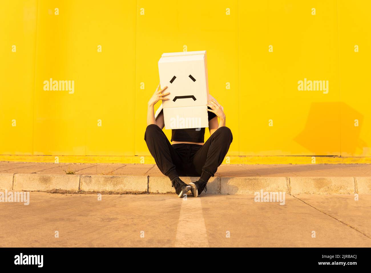 Woman wearing box with sad face sitting in front of yellow wall Stock ...
