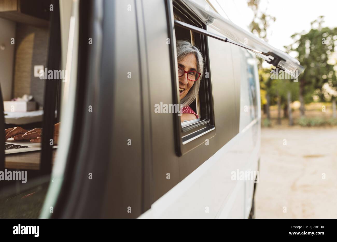 Smiling mature woman looking out of camper van window Stock Photo - Alamy