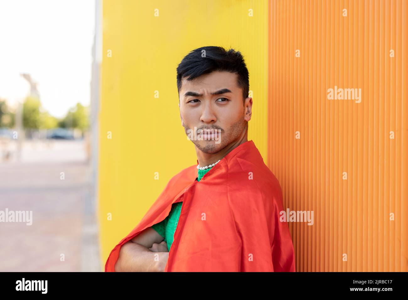 Contemplative young man wearing red cape standing in front of wall ...