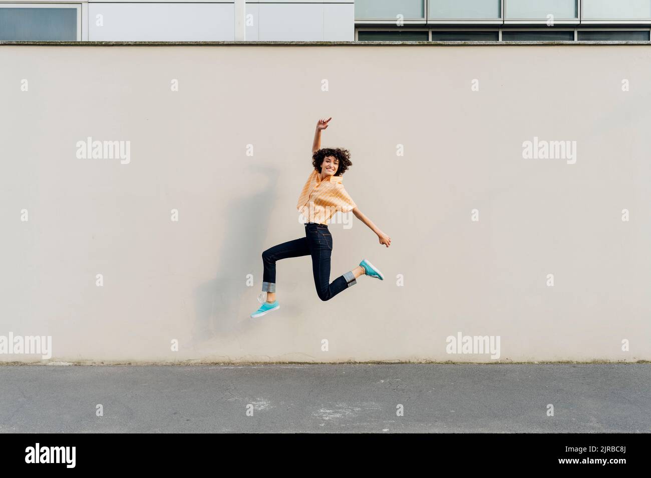Cheerful woman jumping in front of wall Stock Photo - Alamy