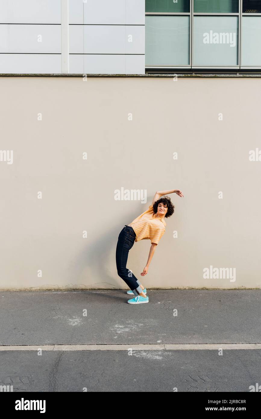 Woman with hand raised bending over backwards in front of wall Stock ...
