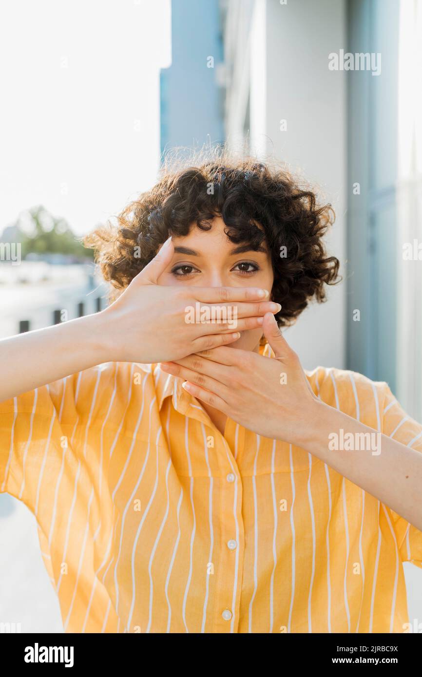 Young woman covering mouth with hands expressing shock Stock Photo - Alamy