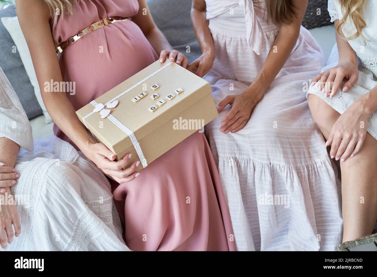 Hands of pregnant woman opening gift box sitting with friends at home ...
