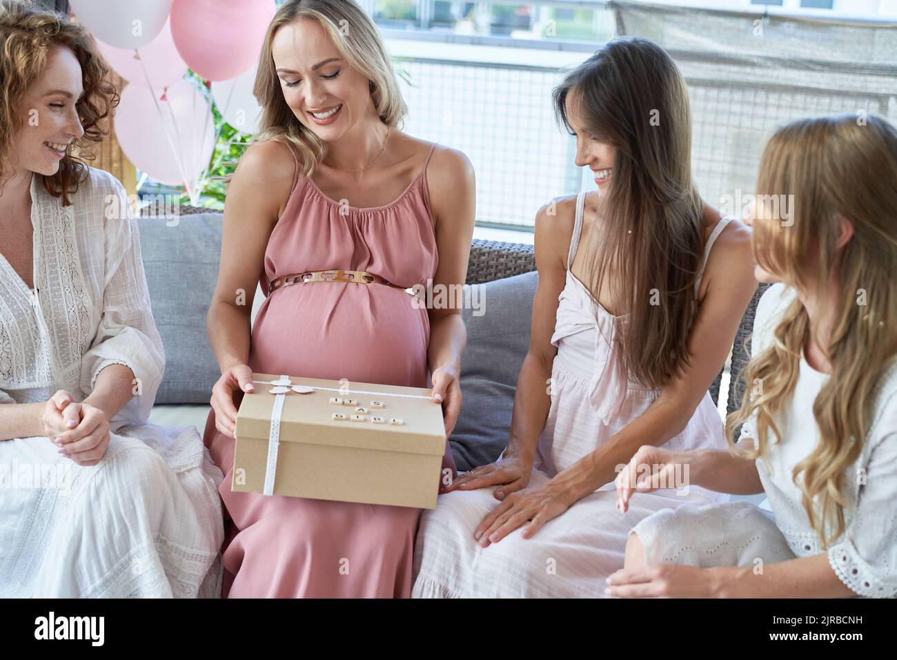 Smiling pregnant woman opening gift box by friends on sofa Stock Photo ...