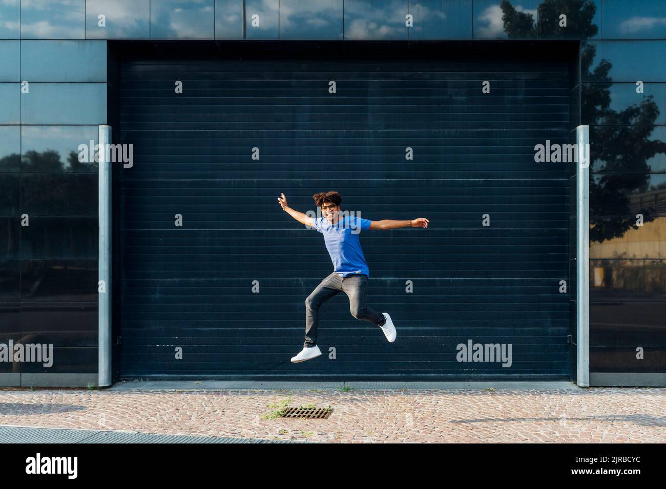 Smiling man jumping in front of building Stock Photo - Alamy