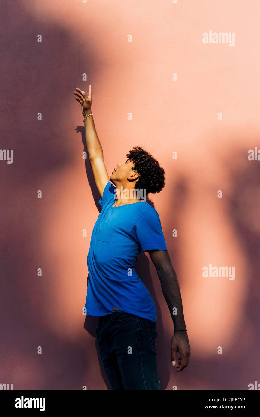 Young man with hand raised standing in front of wall Stock Photo - Alamy