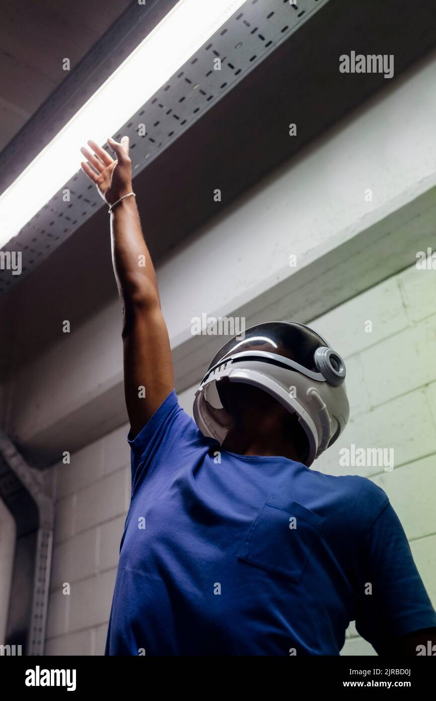 Young man wearing astronaut helmet raising hand reaching LED light ...