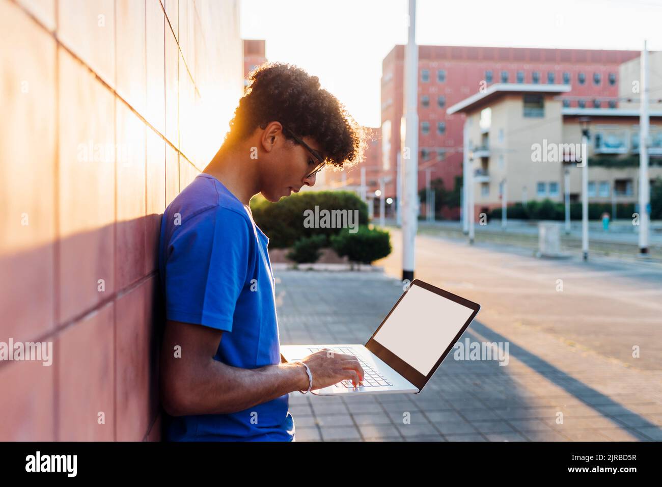 Young man studying through laptop leaning on wall Stock Photo - Alamy
