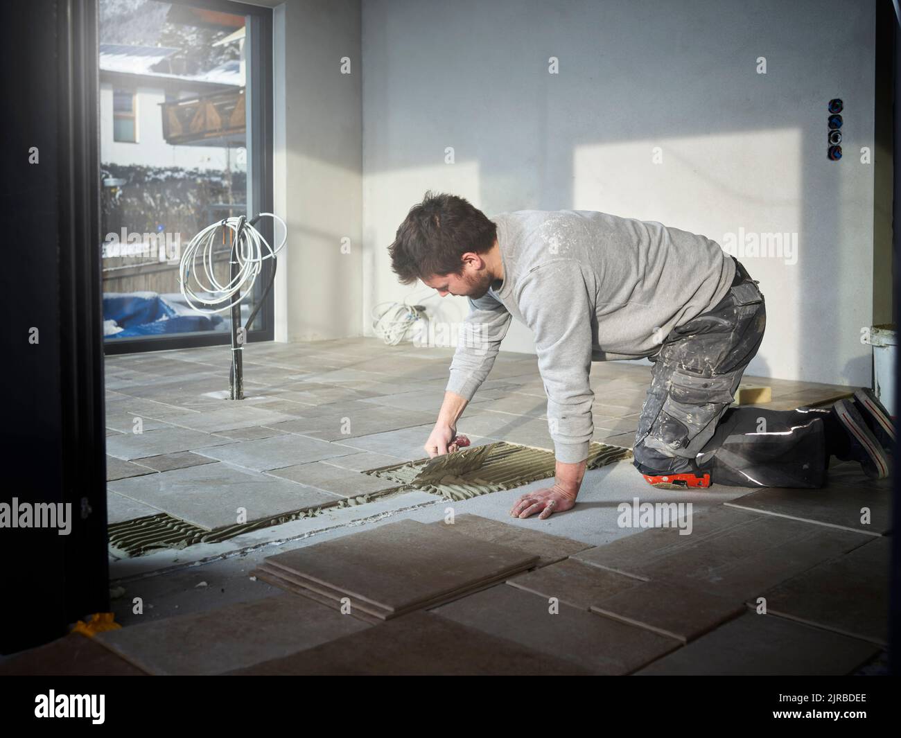 Young tiler applying adhesive on floor at construction site Stock Photo ...