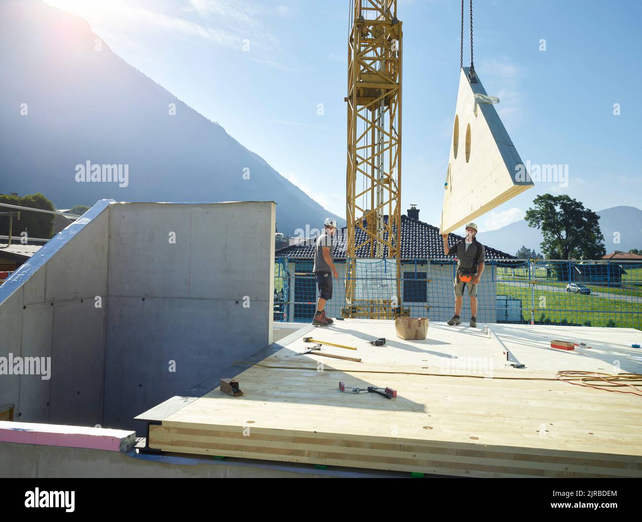 Colleagues working on rooftop with help of crane at construction site ...