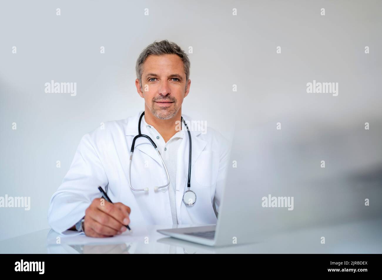 Portrait of mature doctor sitting at desk in medical practice Stock ...