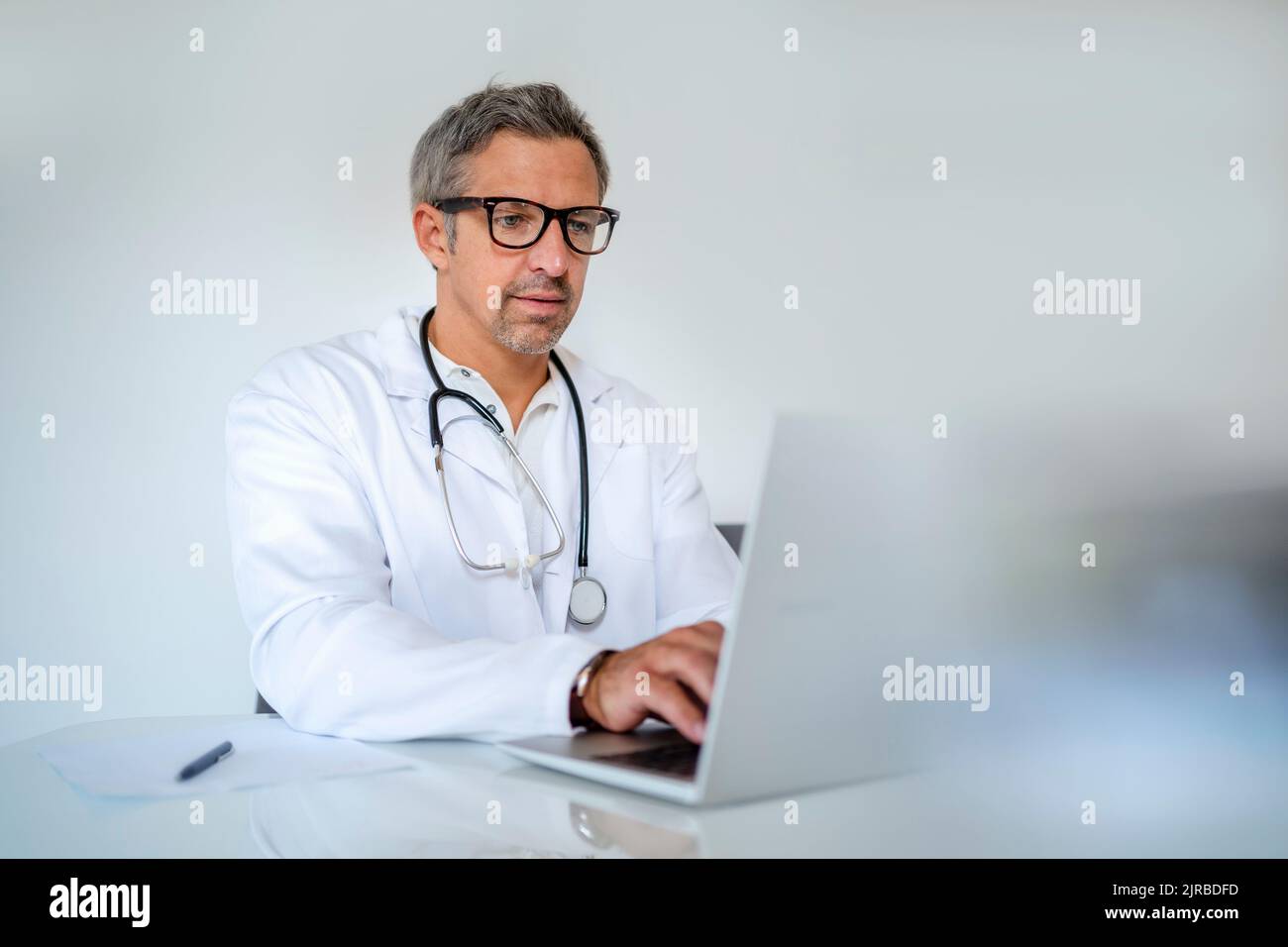 Mature doctor using laptop at desk in medical practice Stock Photo - Alamy