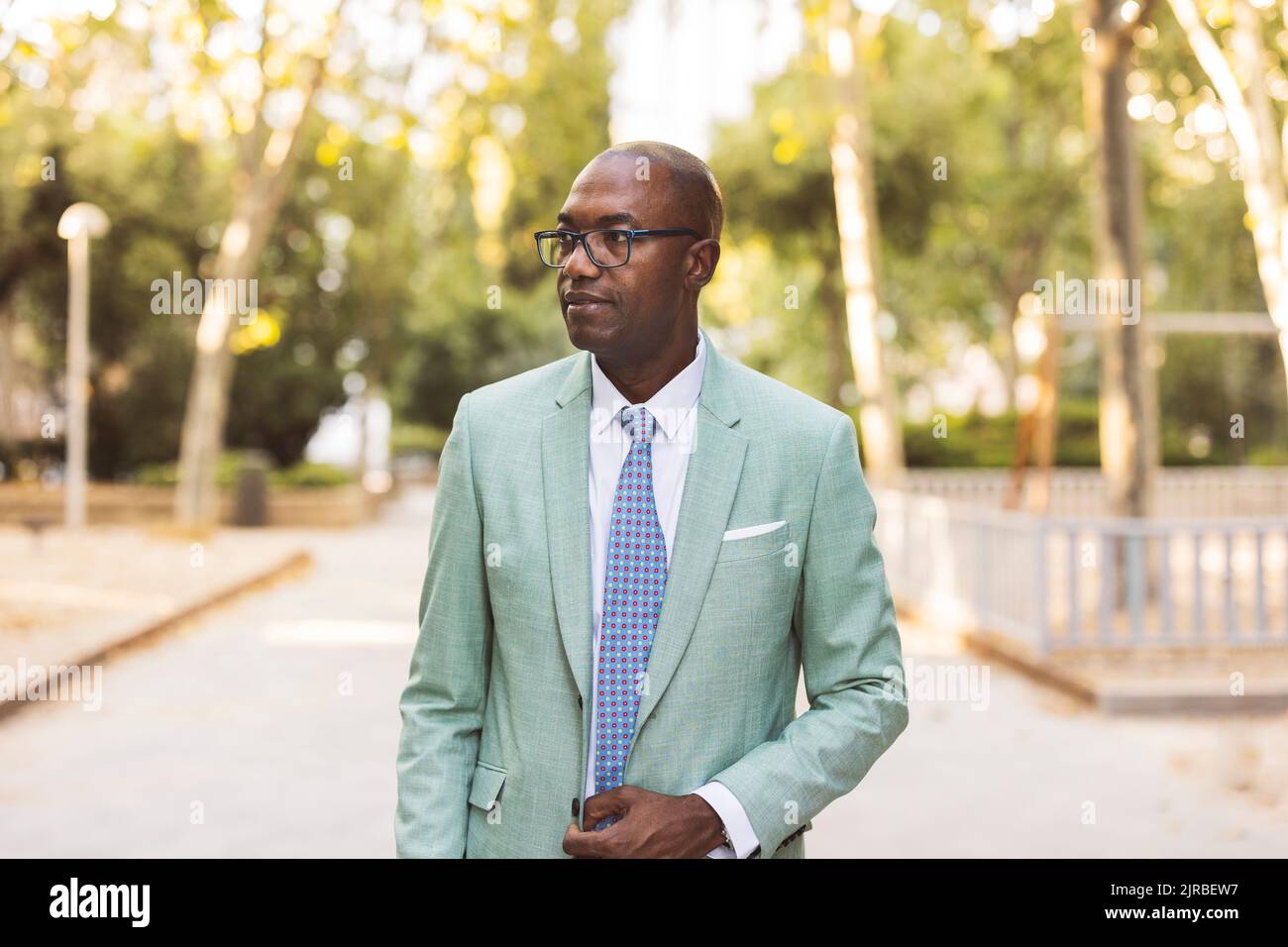 Mature businessman wearing eyeglasses and businesswear standing in park ...