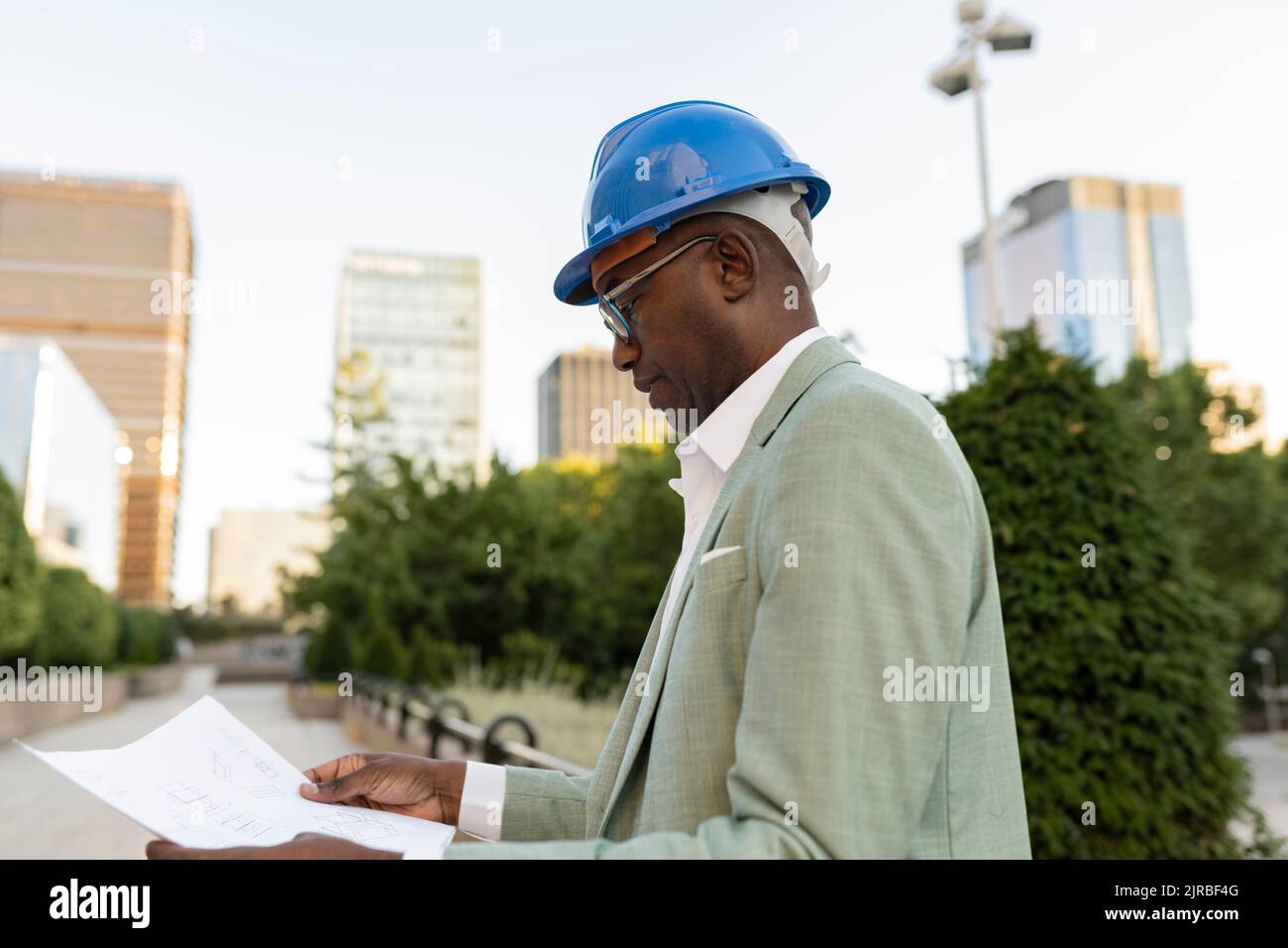 Engineer wearing hardhat examining blueprint at financial district ...