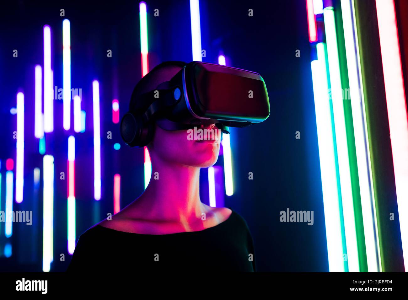 Woman wearing virtual reality simulator near colorful illuminated ...