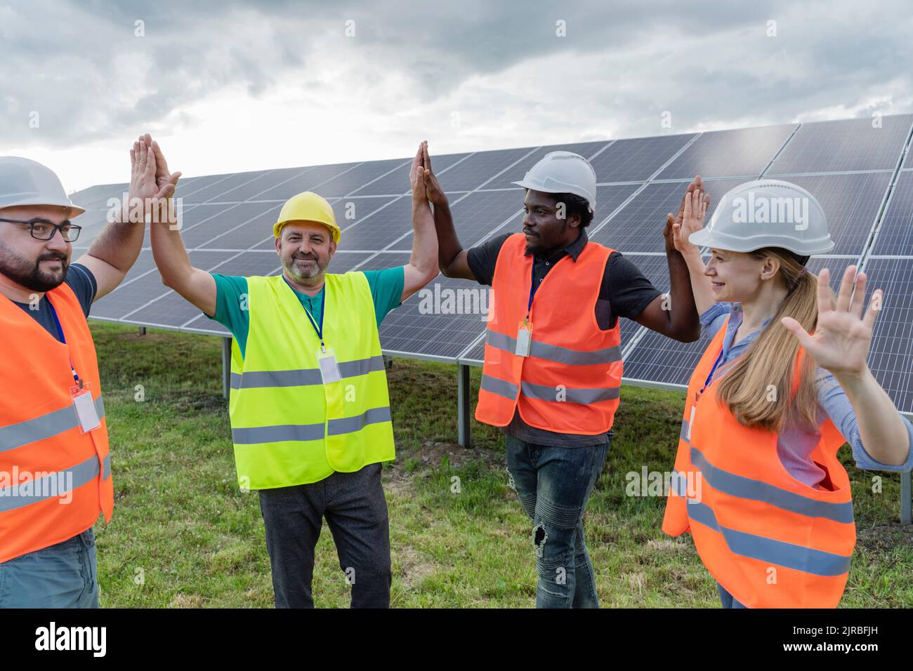 Smiling engineers high-fiving and standing in front of solar panels at ...