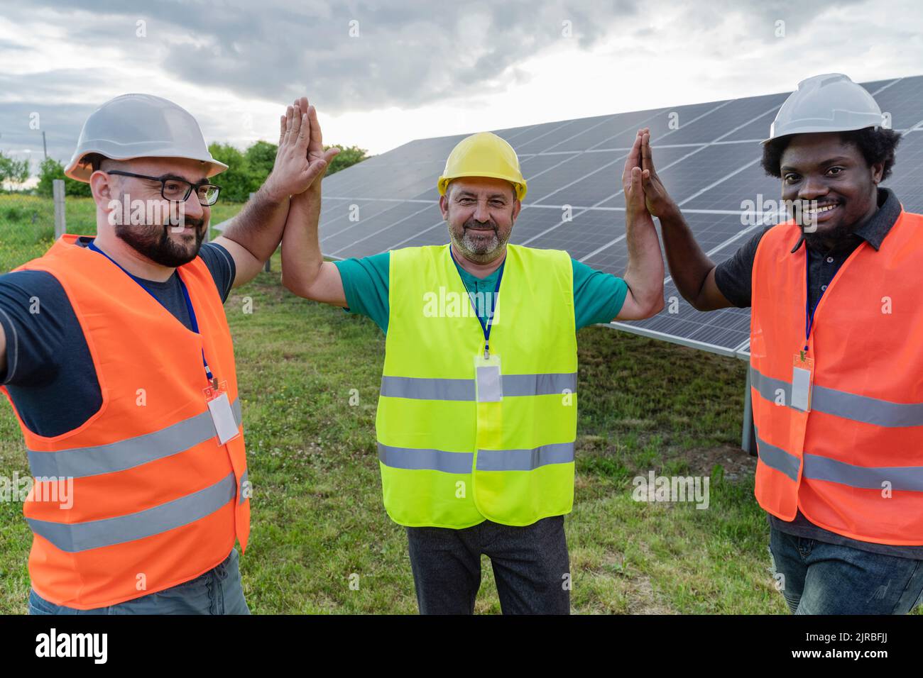 Smiling engineers giving high five to each other at solar power station ...