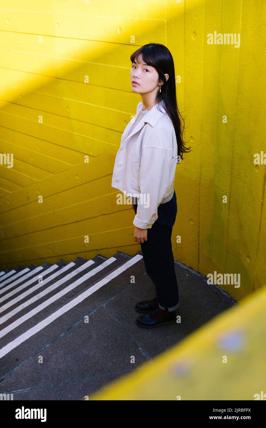 Young woman standing in front of steps by yellow wall Stock Photo - Alamy