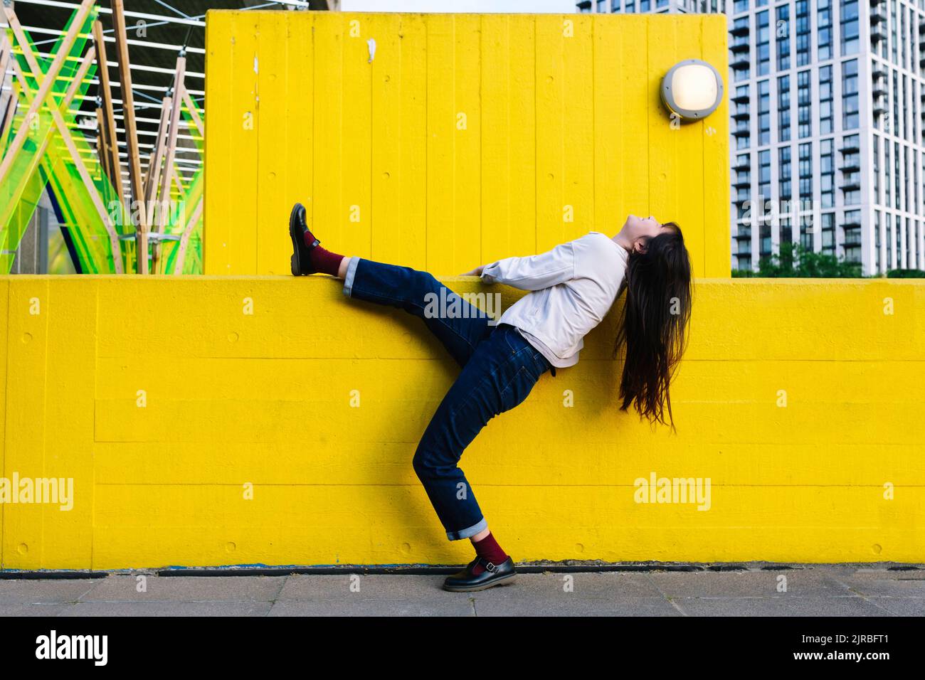 Young woman leaning backwards standing on one leg by wall Stock Photo ...