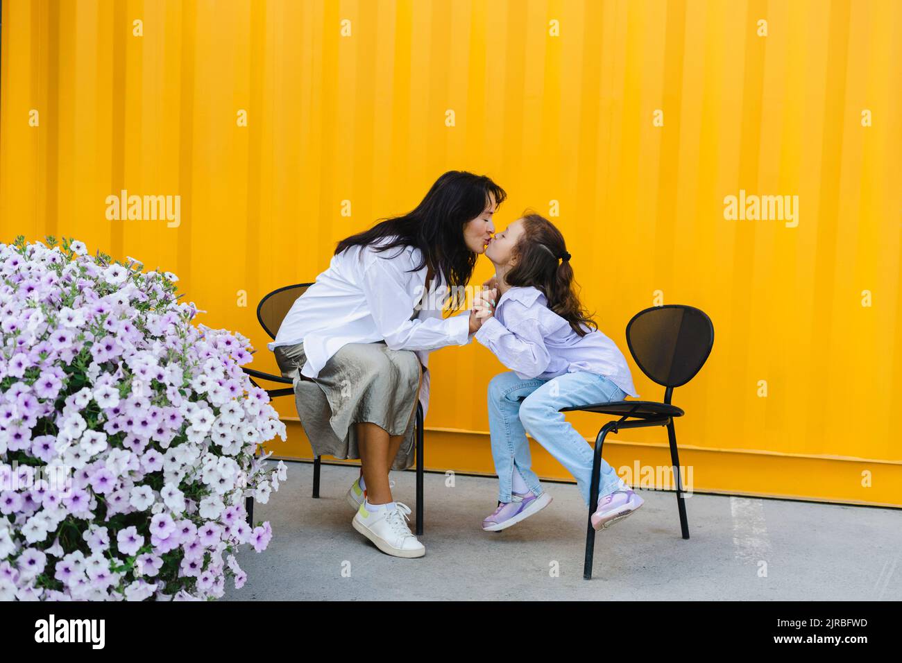 Affectionate mother kissing daughter on mouth in front of yellow wall ...