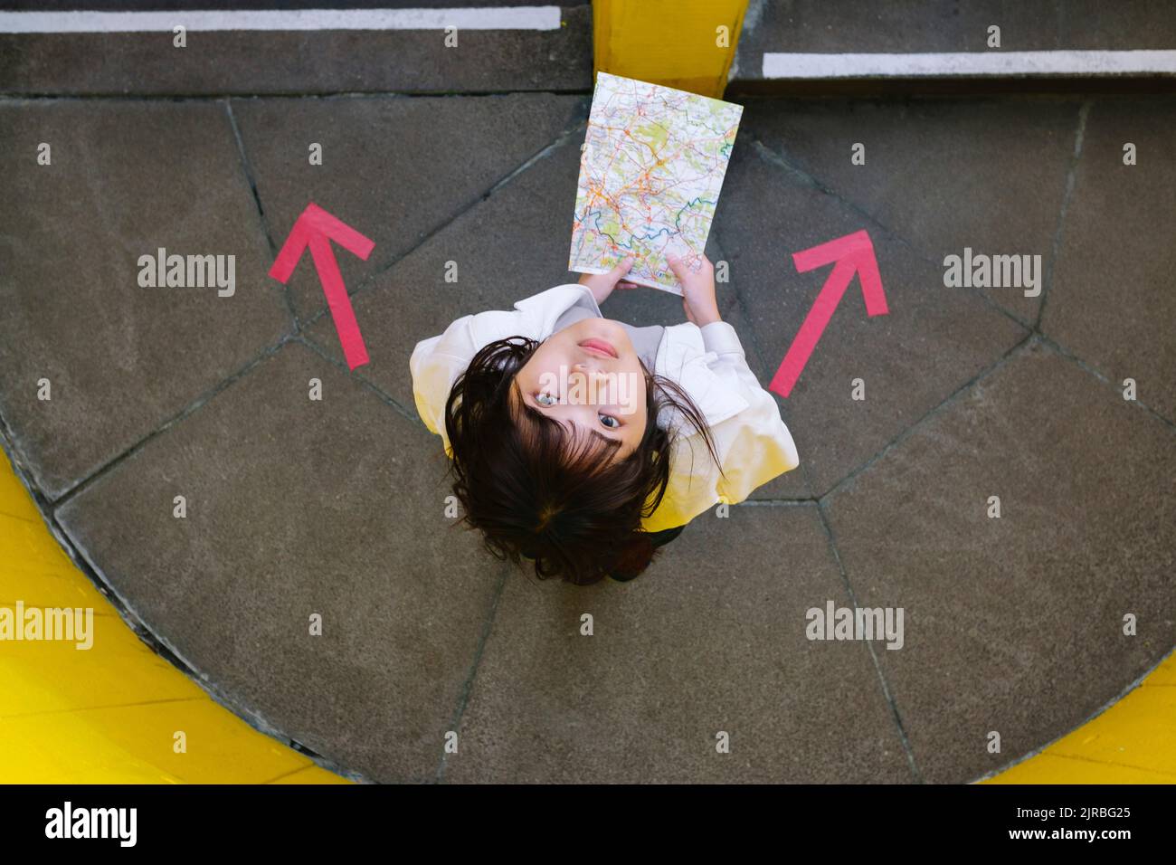Young woman looking up holding map standing by arrow symbols Stock ...