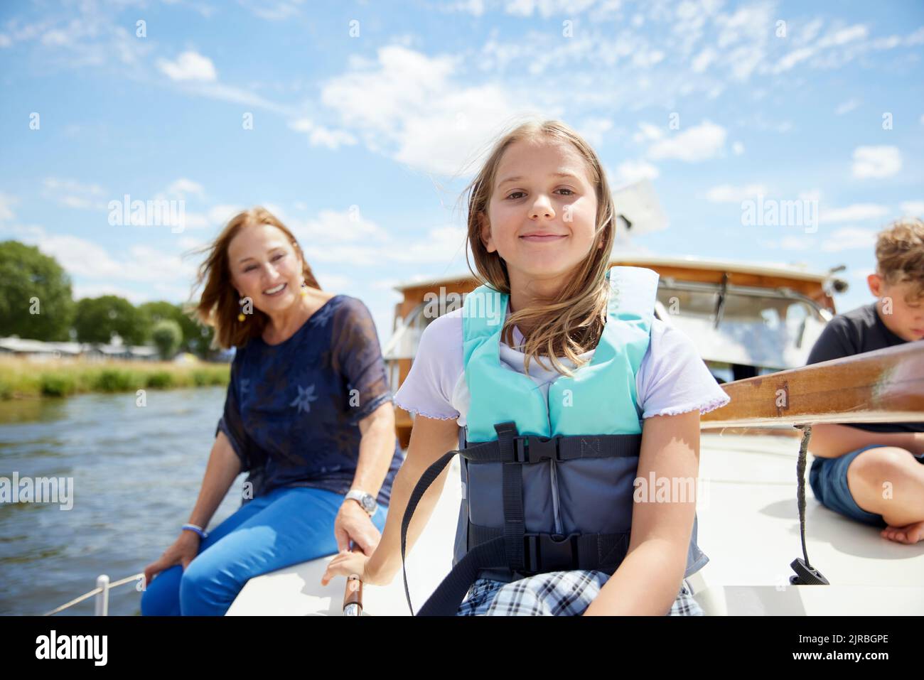 Smiling girl wearing life jacket sitting on boat deck with family at ...