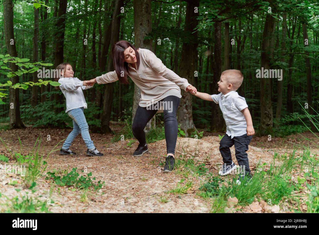 Happy children pulling mother having fun in forest Stock Photo - Alamy