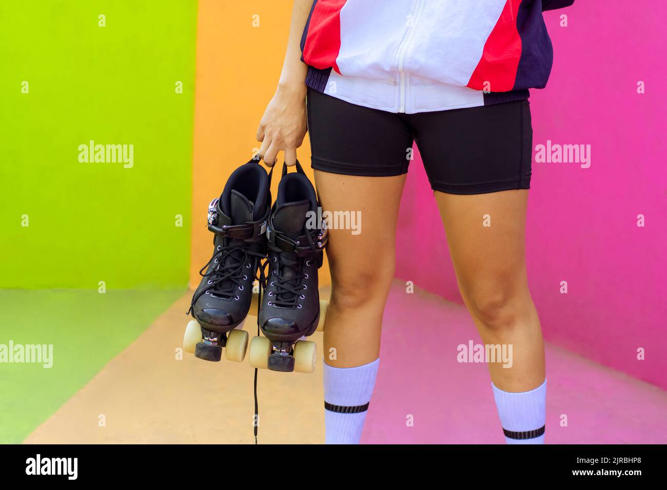 Woman holding roller skates standing in front of multi colored wall ...