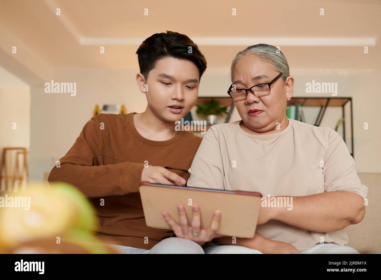 Vietnamese teenage boy showing grandmother how to use tablet computer ...