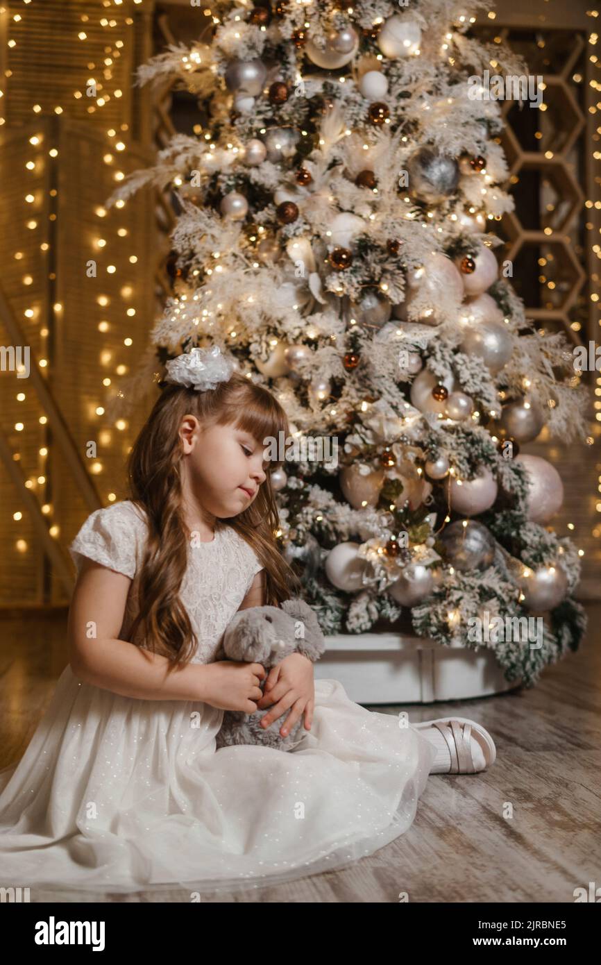 A girl in a festive light dress next to a Christmas tree, lights of ...