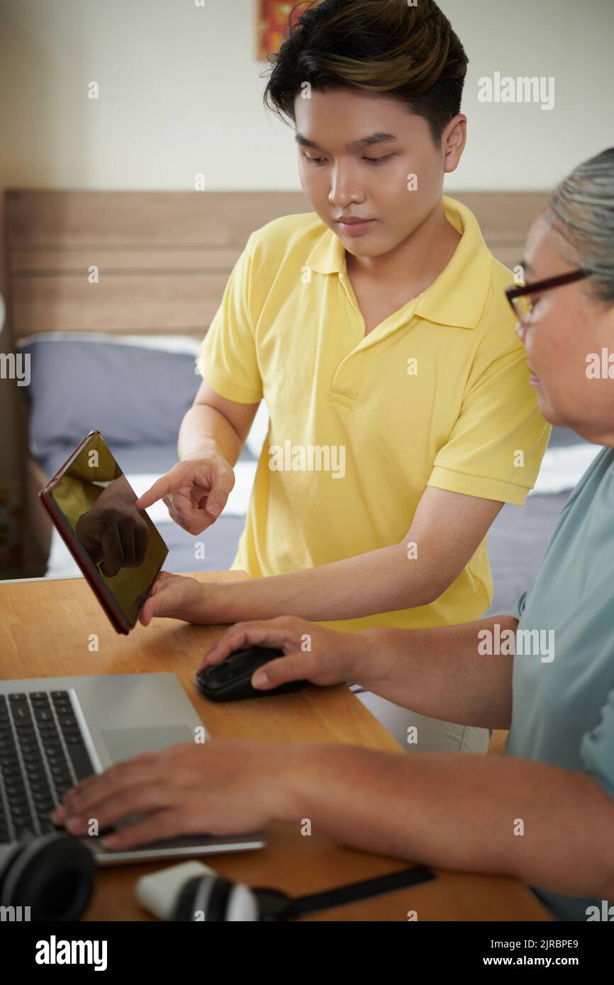 Teenage Vietnamese boy explaining grandmother how to use application on ...