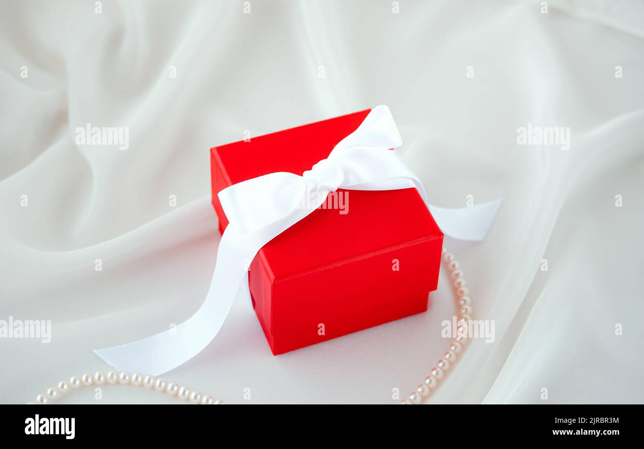 Red gift box with white ribbon on white silk background Stock Photo - Alamy