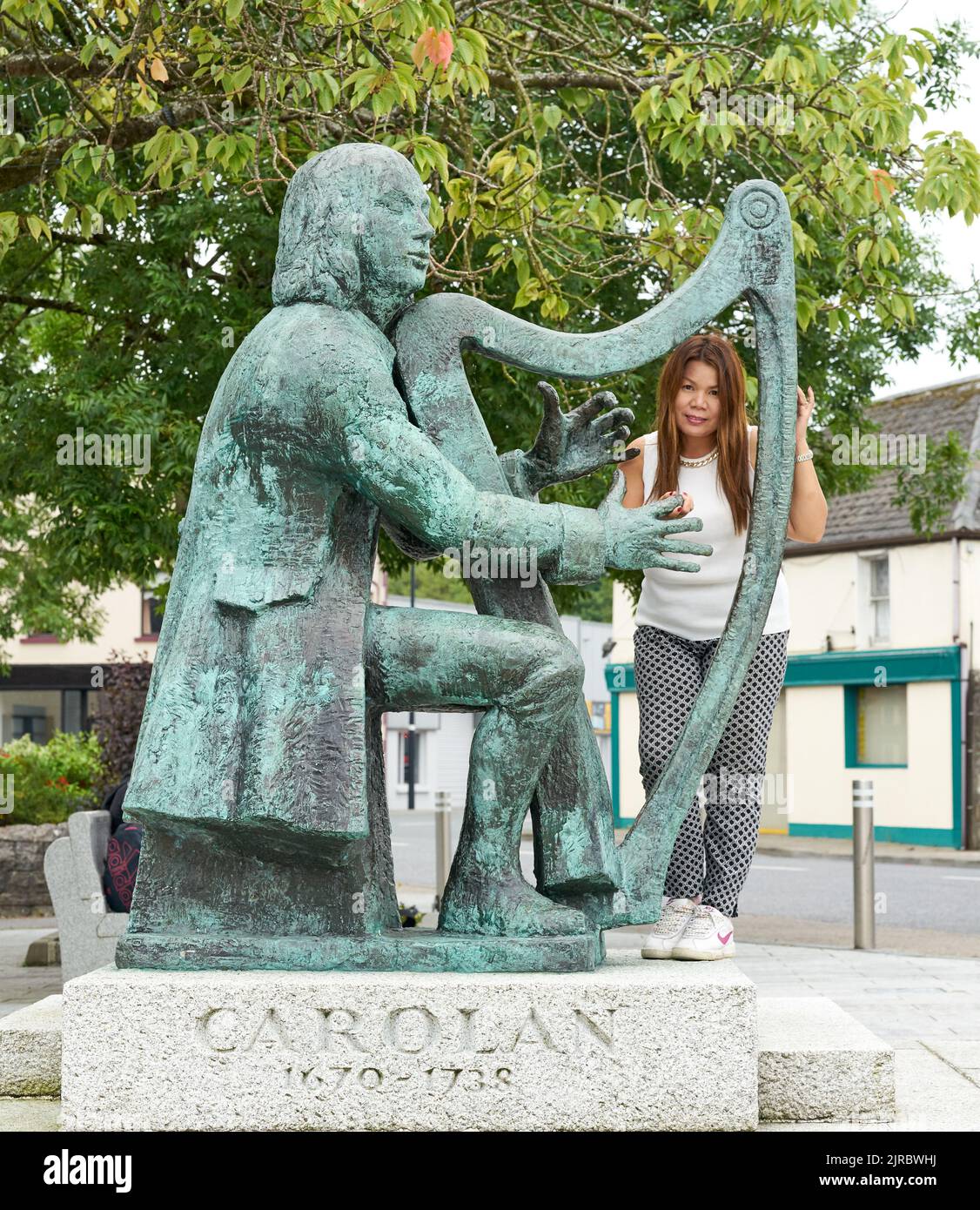 A pretty lady poses by a statue of a statue of an Irish harpist in Ireland Stock Photo - Alamy