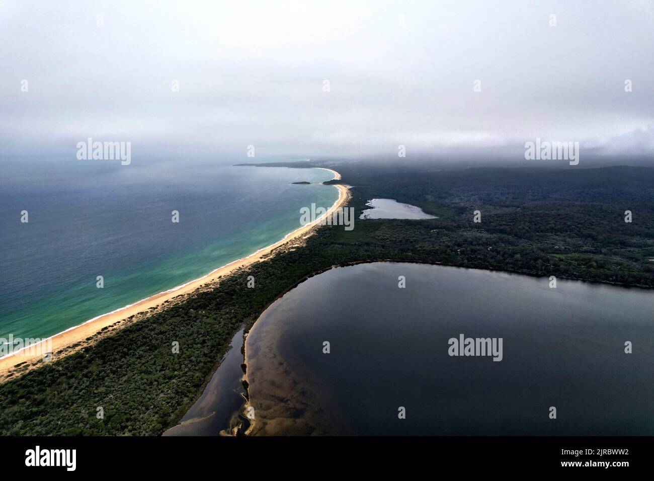 An aerial view of a white sand beach surrounded by bushland with a lake ...