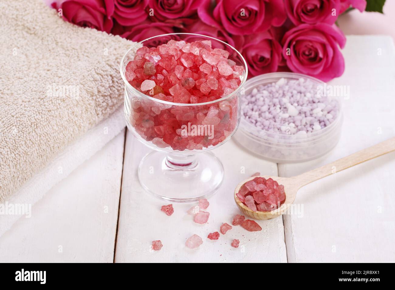 Glass bowl with red sea salt. Pink roses in the background. Spa time ...
