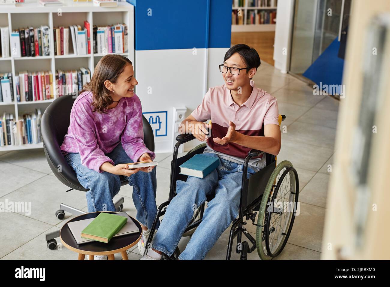 High angle portrait of Asian young man in wheelchair talking to friend ...