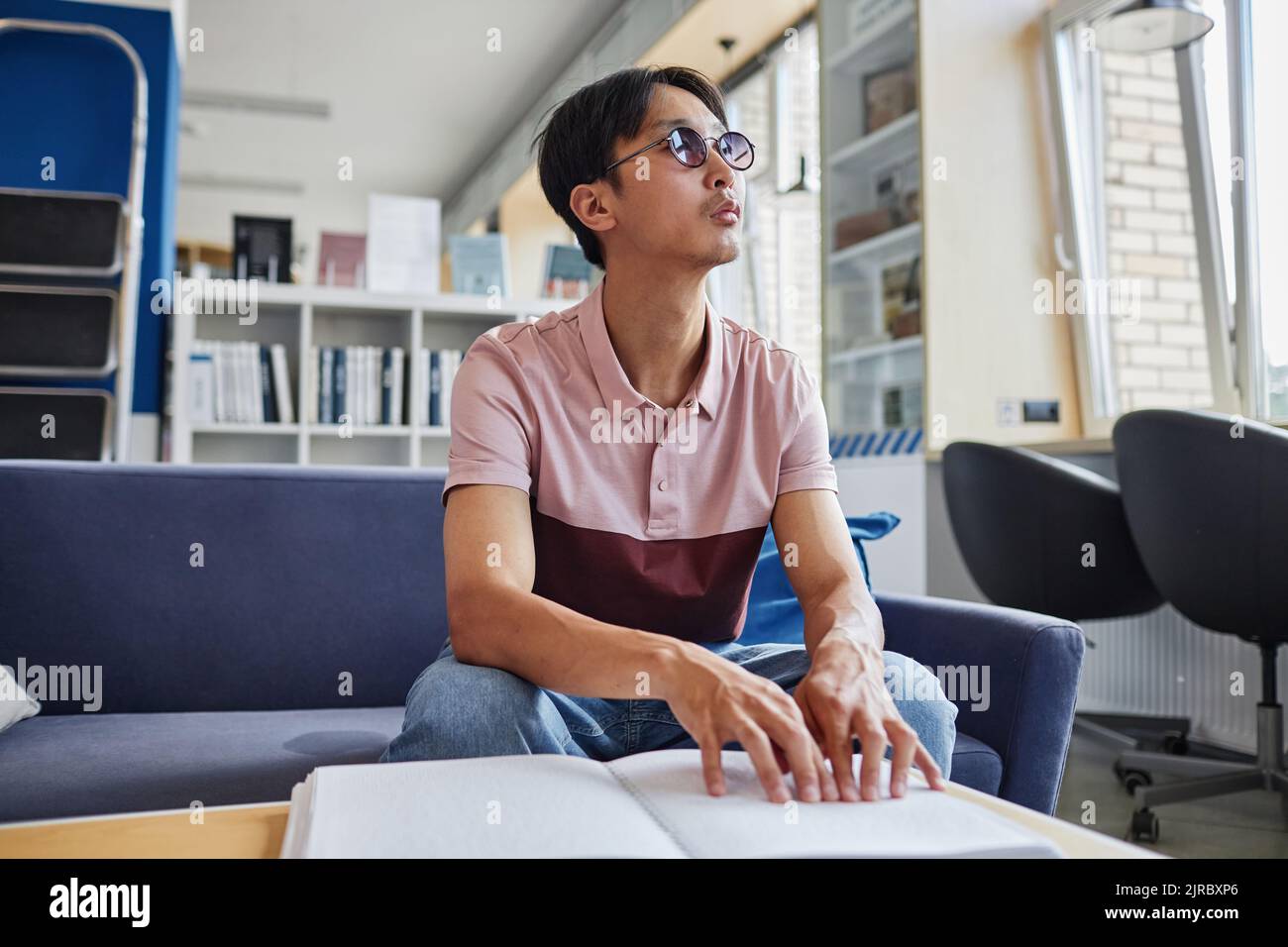 Low angle portrait of Asian young man reading book in tactile braille ...