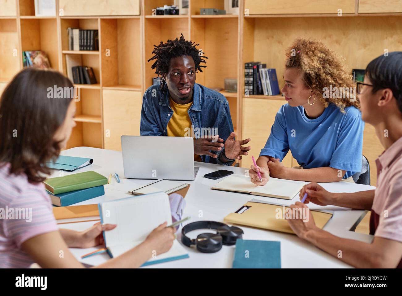 Diverse group of young students working on project together while ...