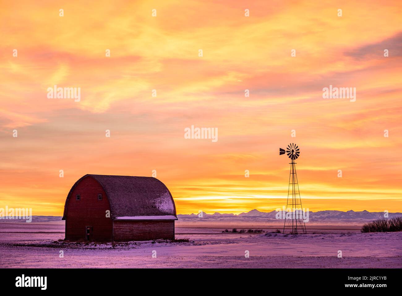 A wooden barn and wind mill silhouetted by a winter sunset in rural ...