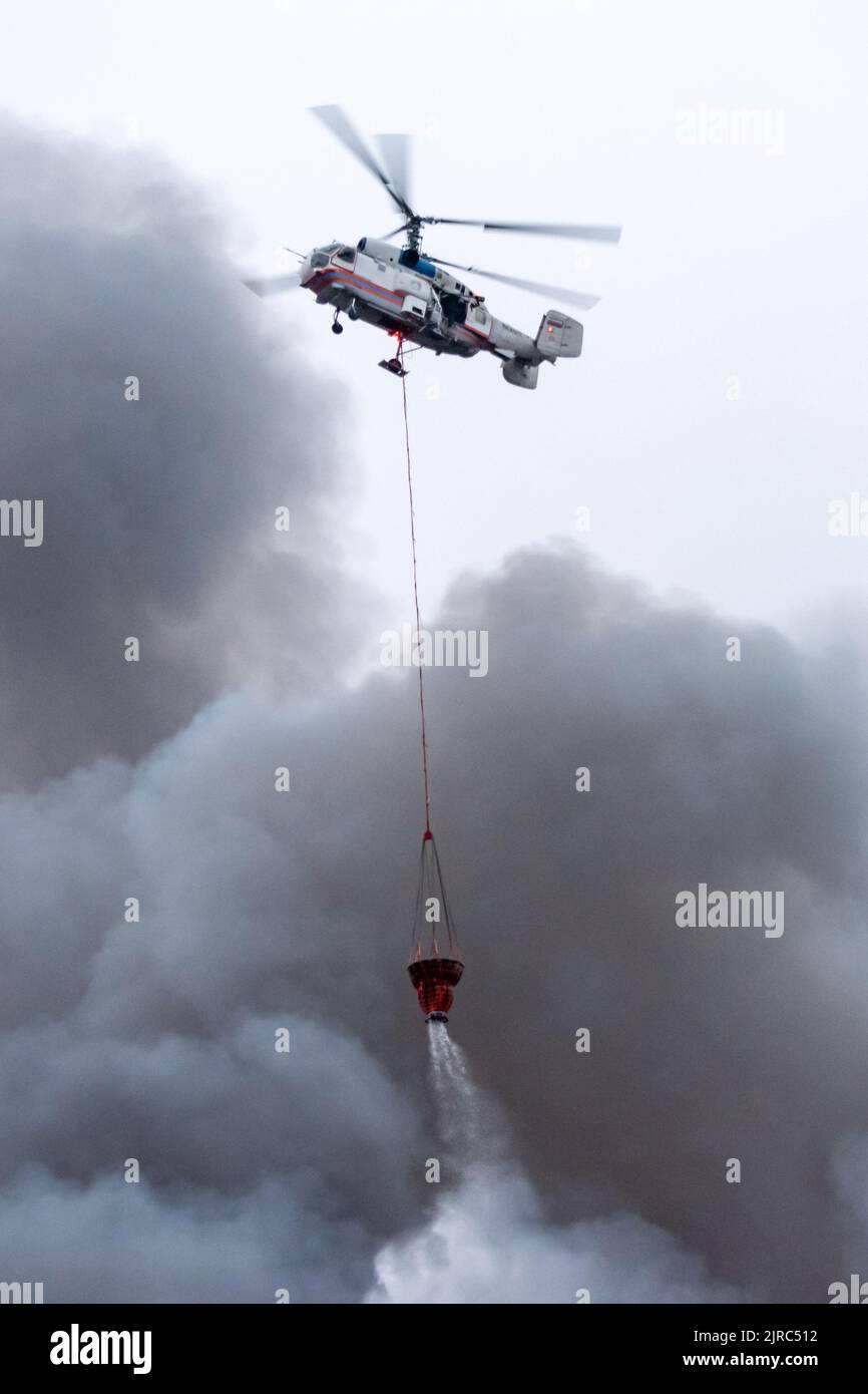 A fire helicopter carries a container of water to extinguish a fire in ...