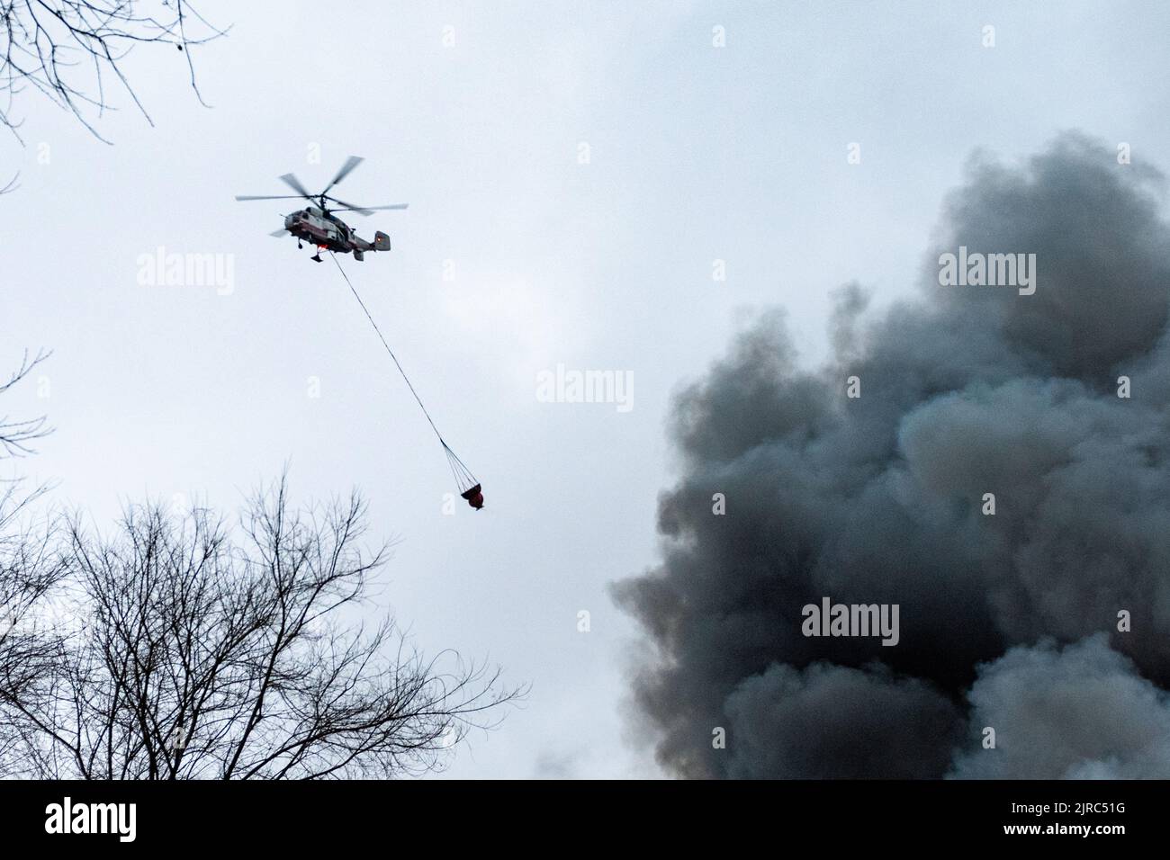 A fire helicopter carries a container of water to extinguish a fire in ...