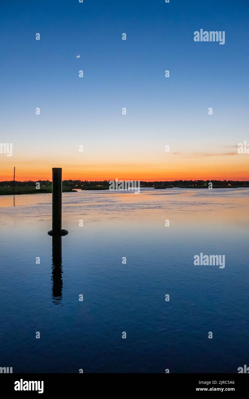 Crescent moon hangs in a blue sky vibrant sunset above a post in the ...