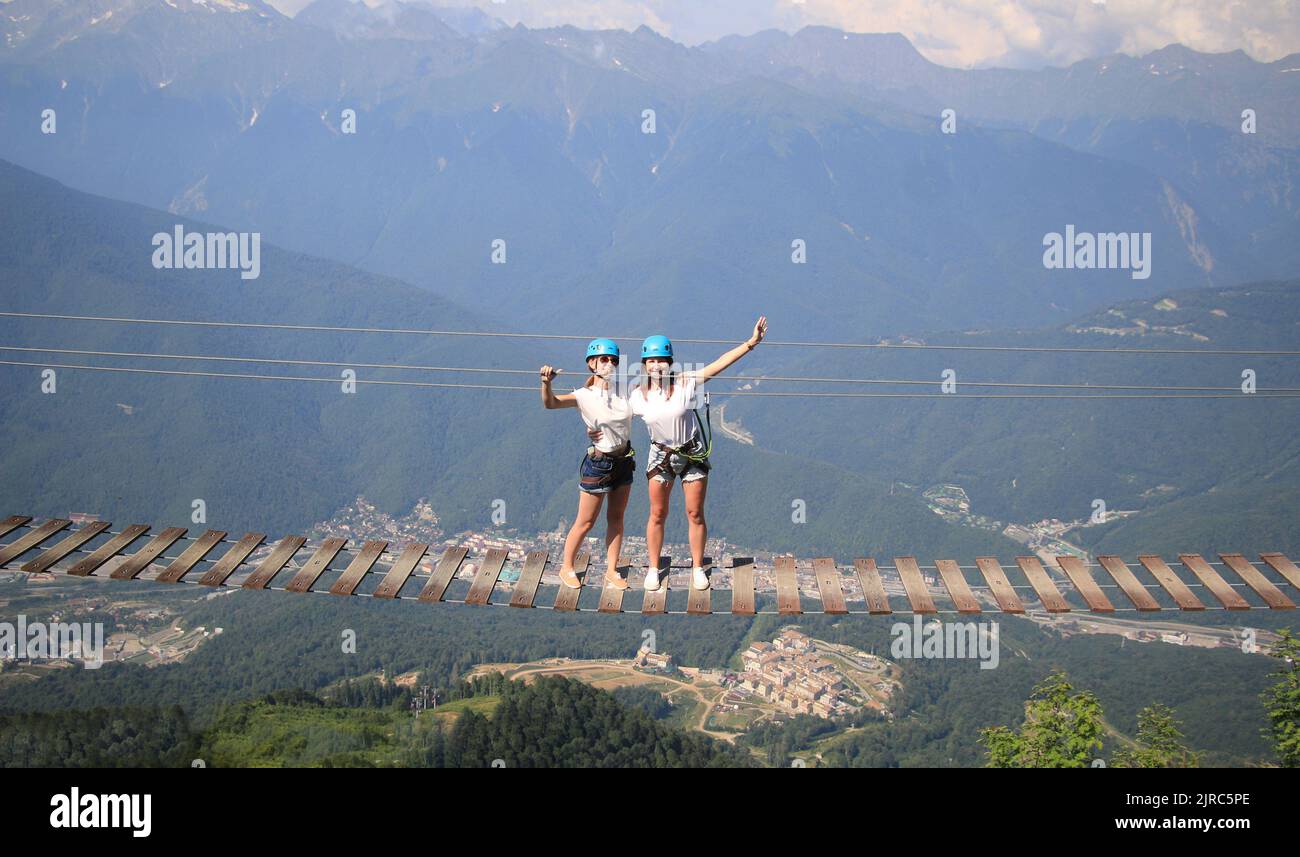 Two happy girls stand on a rope bridge in the mountains. Extreme ...