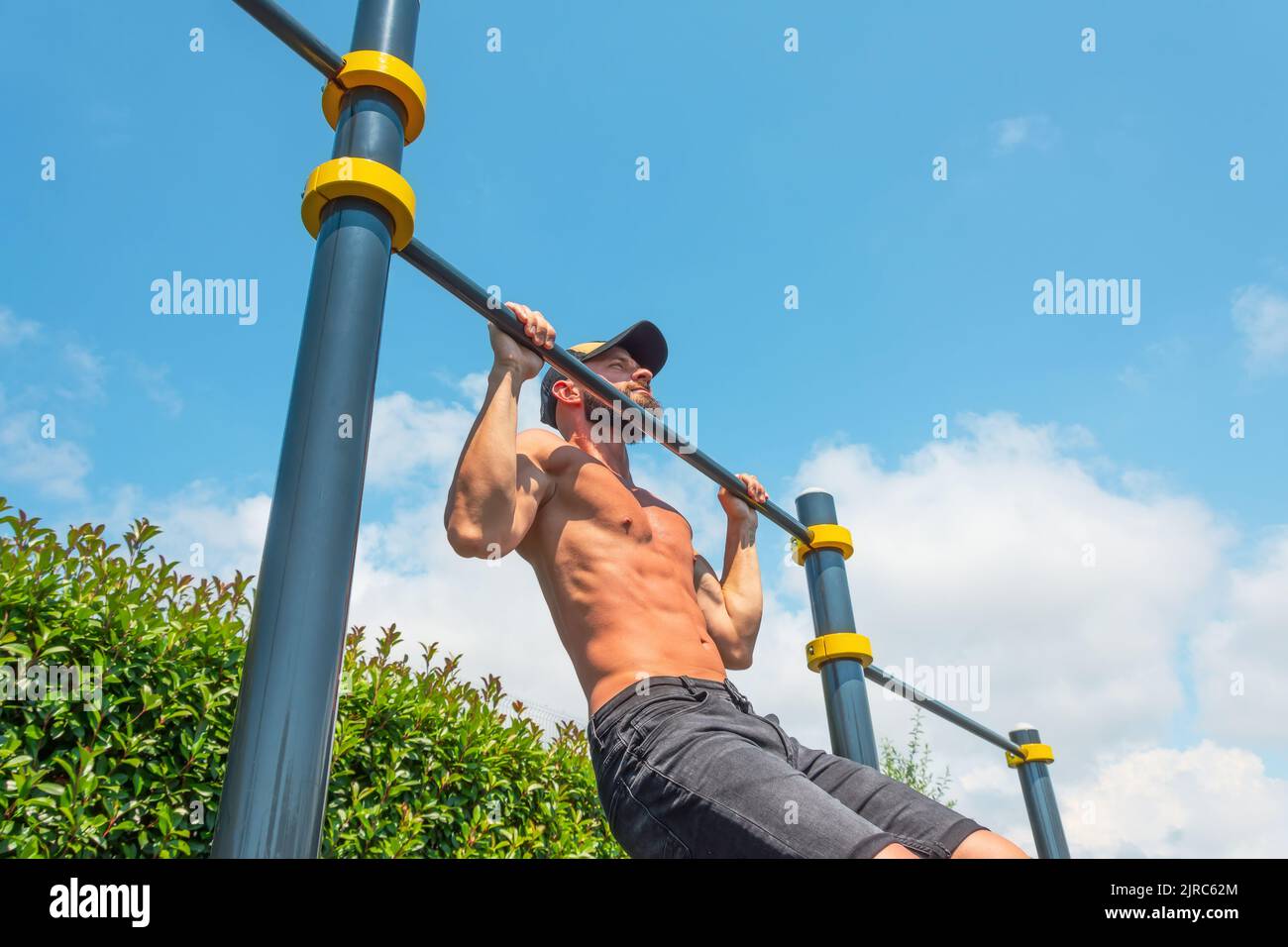 Muscular man in a cap doing pull-ups on the horizontal bar in the park ...