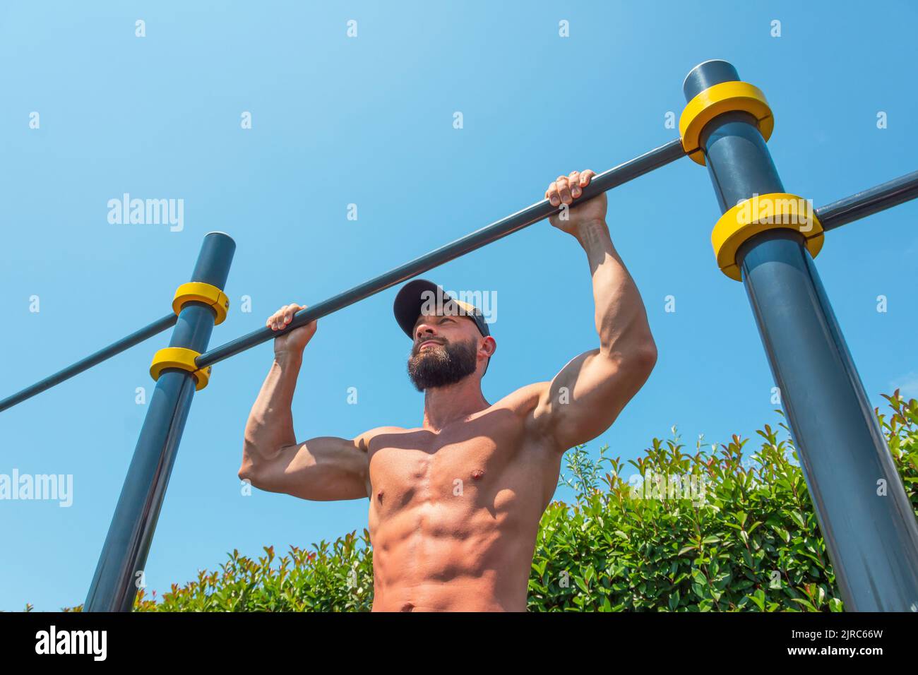 Muscular man in a cap doing pull-ups on the horizontal bar with his ...